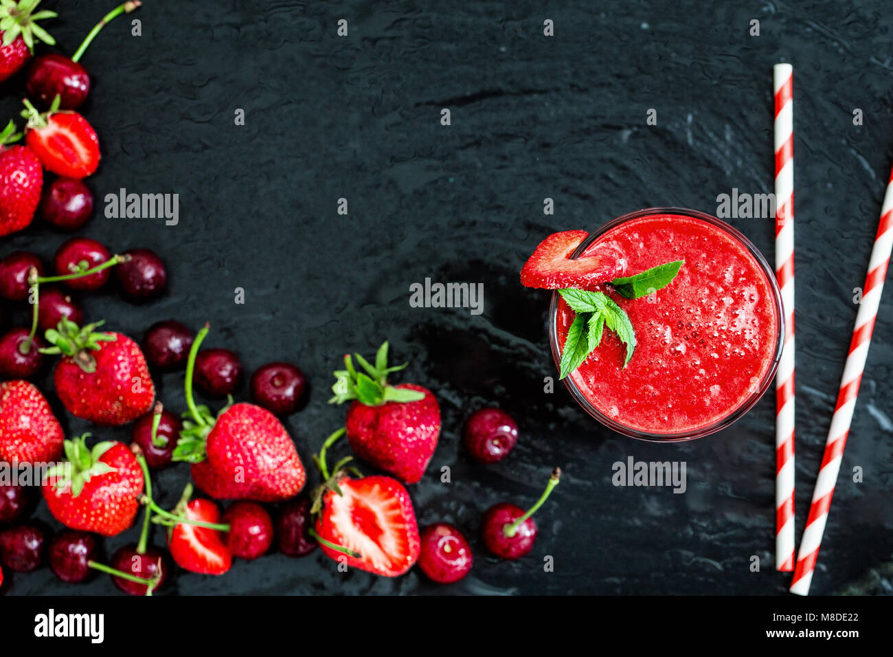 Glass with two straws filled with strawberry smoothie on black with ...