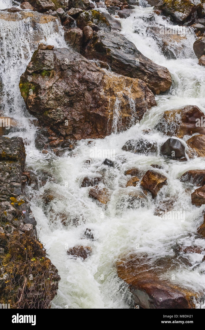 A natural waterfall gushing down the slopes of the Himalayas lined with ...