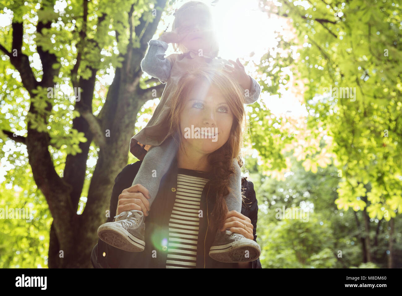 Mother giving toddler daughter shoulder carry in sunlit park Stock ...