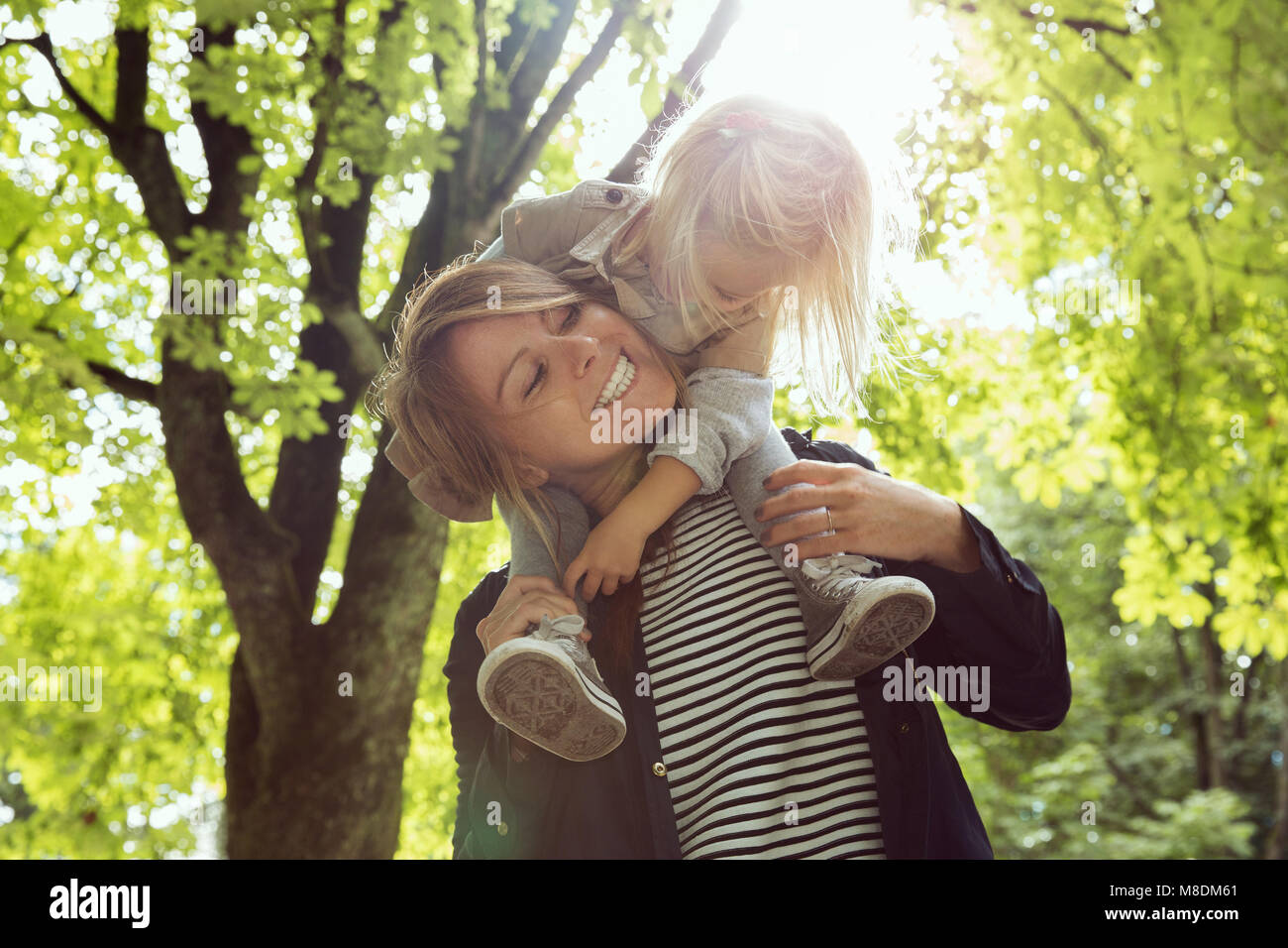 Mother giving toddler daughter shoulder carry in sunlit park Stock ...
