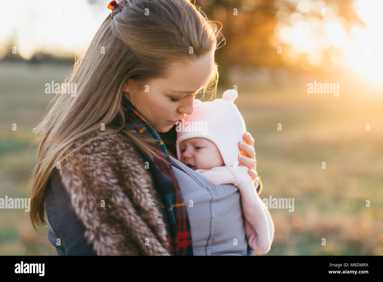 Mother and baby daughter outdoors, mother carrying baby in baby sling ...