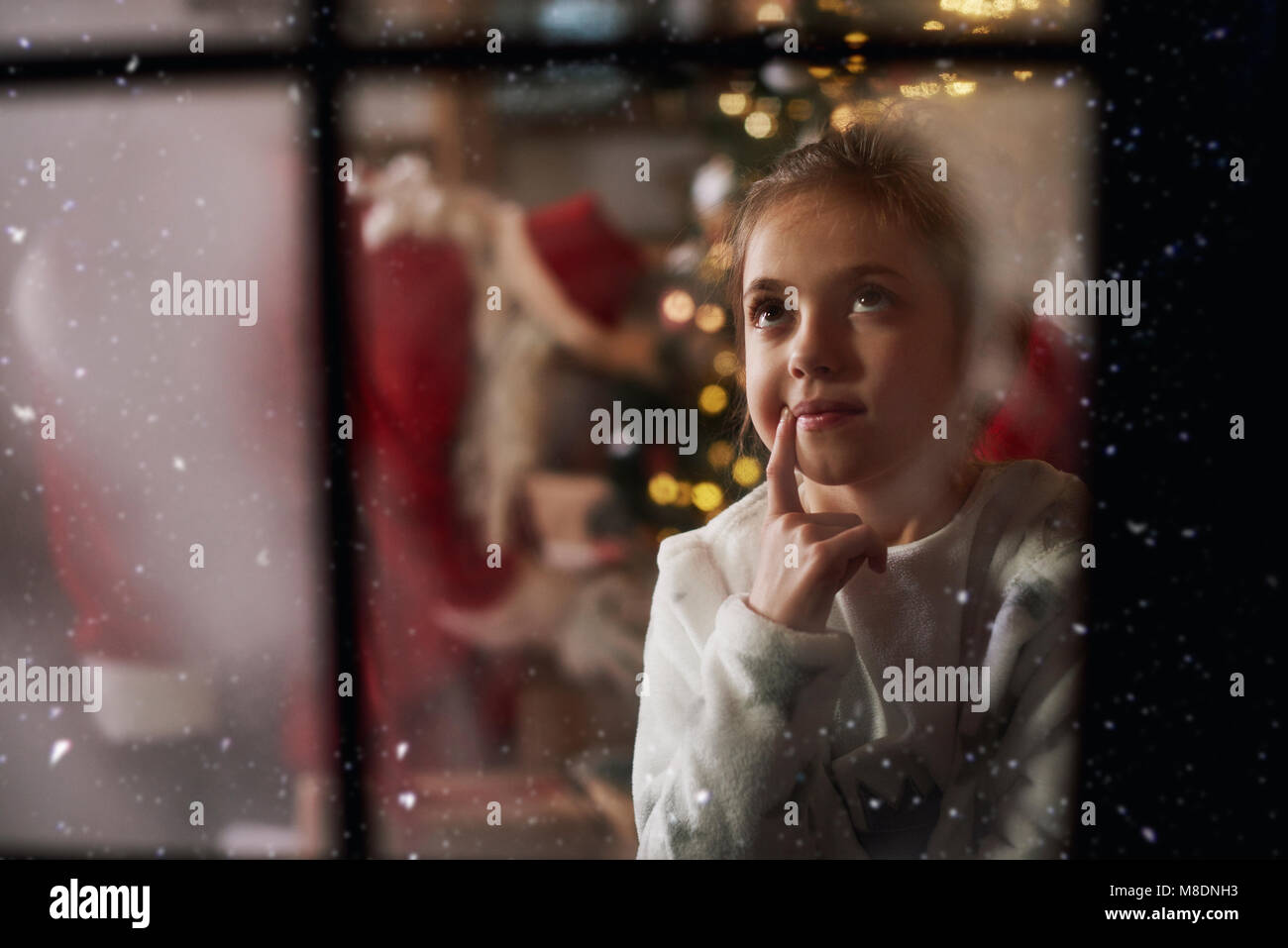 Young girl looking out of window on Christmas eve, Santa in background ...