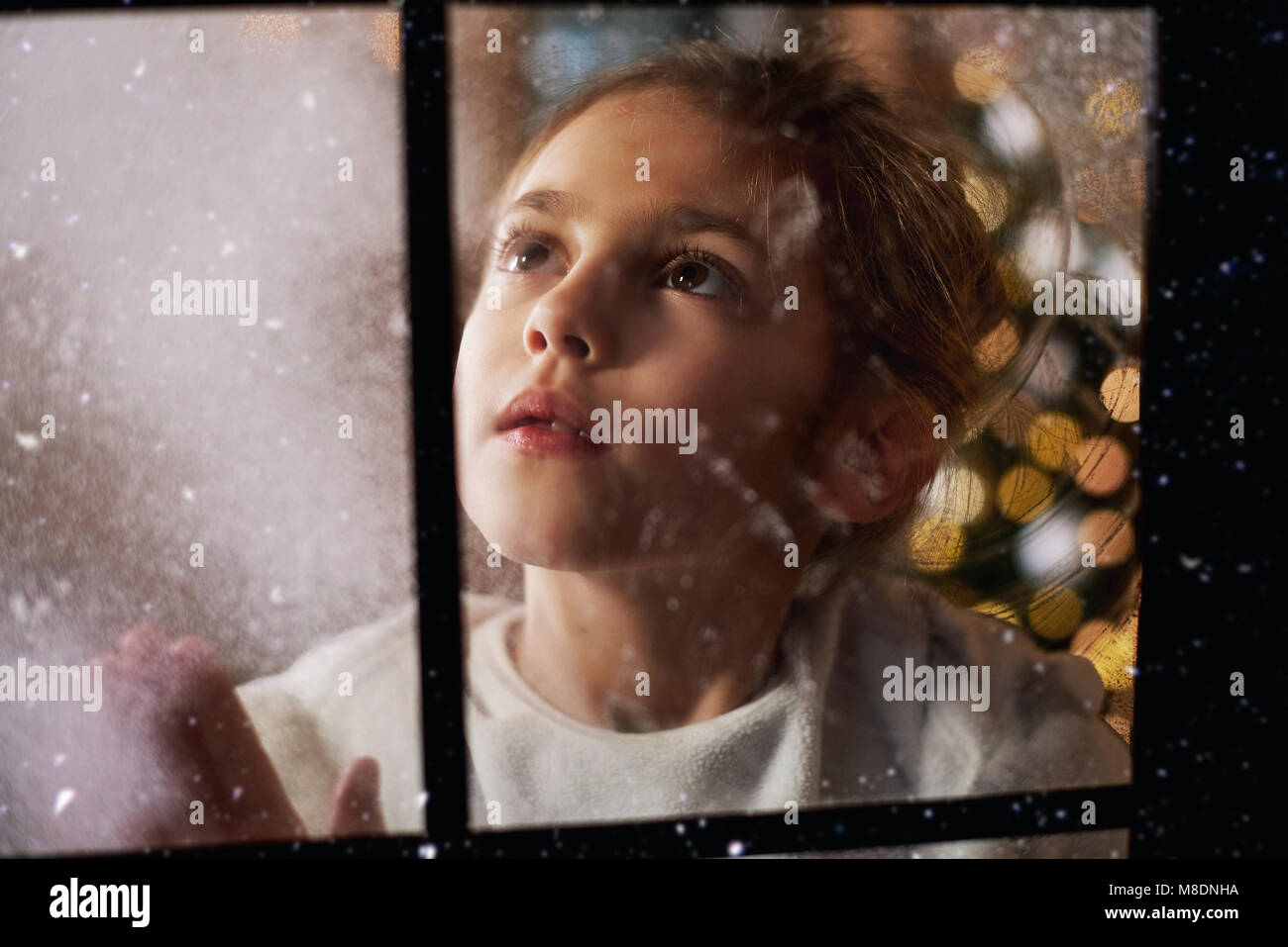 Young girl looking out of window, Christmas tree in background behind ...