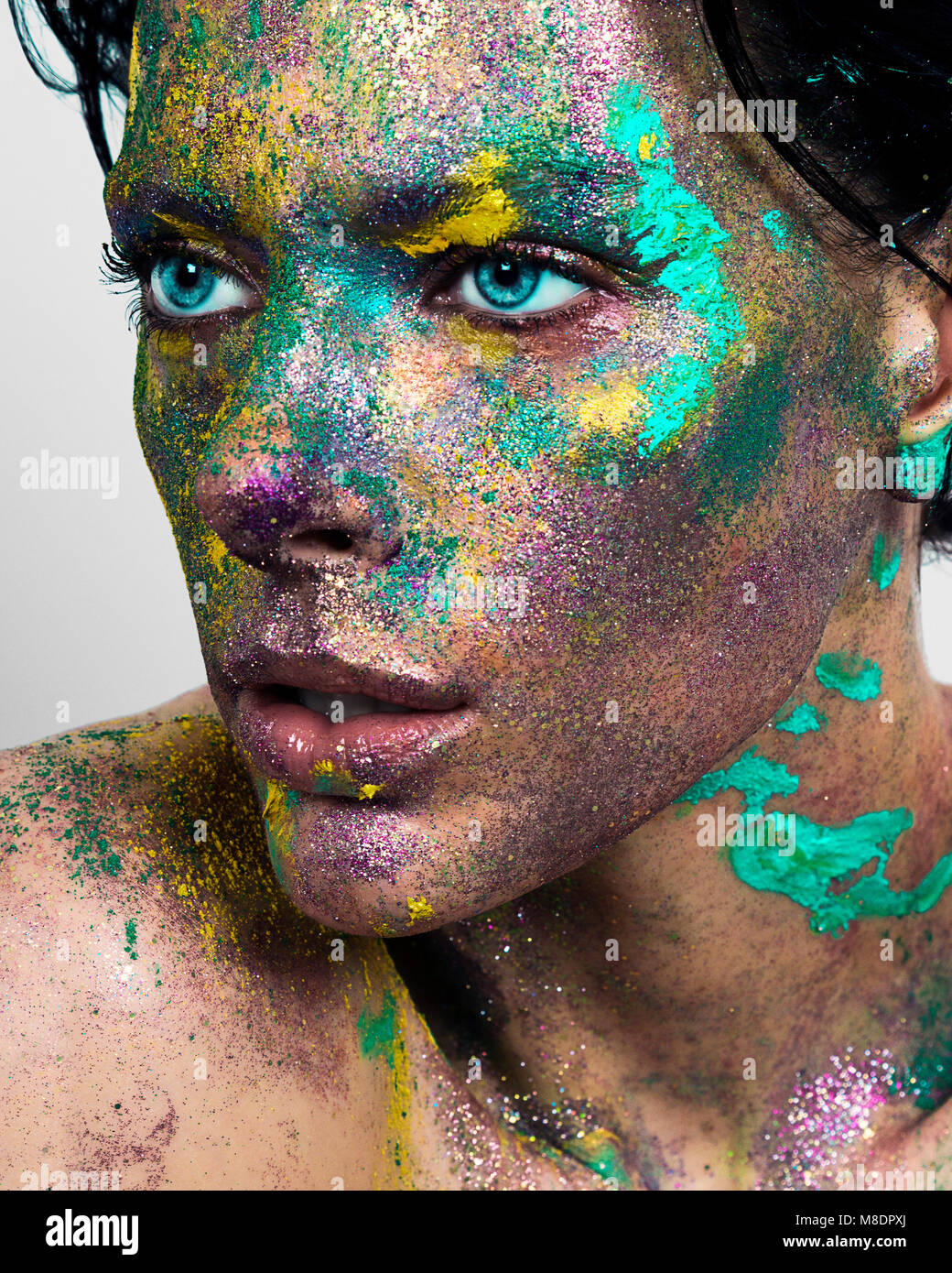 Studio portrait of blue eyed young woman with glittery multi coloured ...