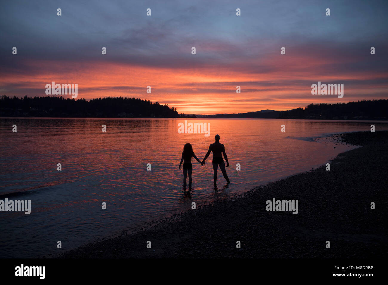 Couple on beach at sunset Stock Photo - Alamy