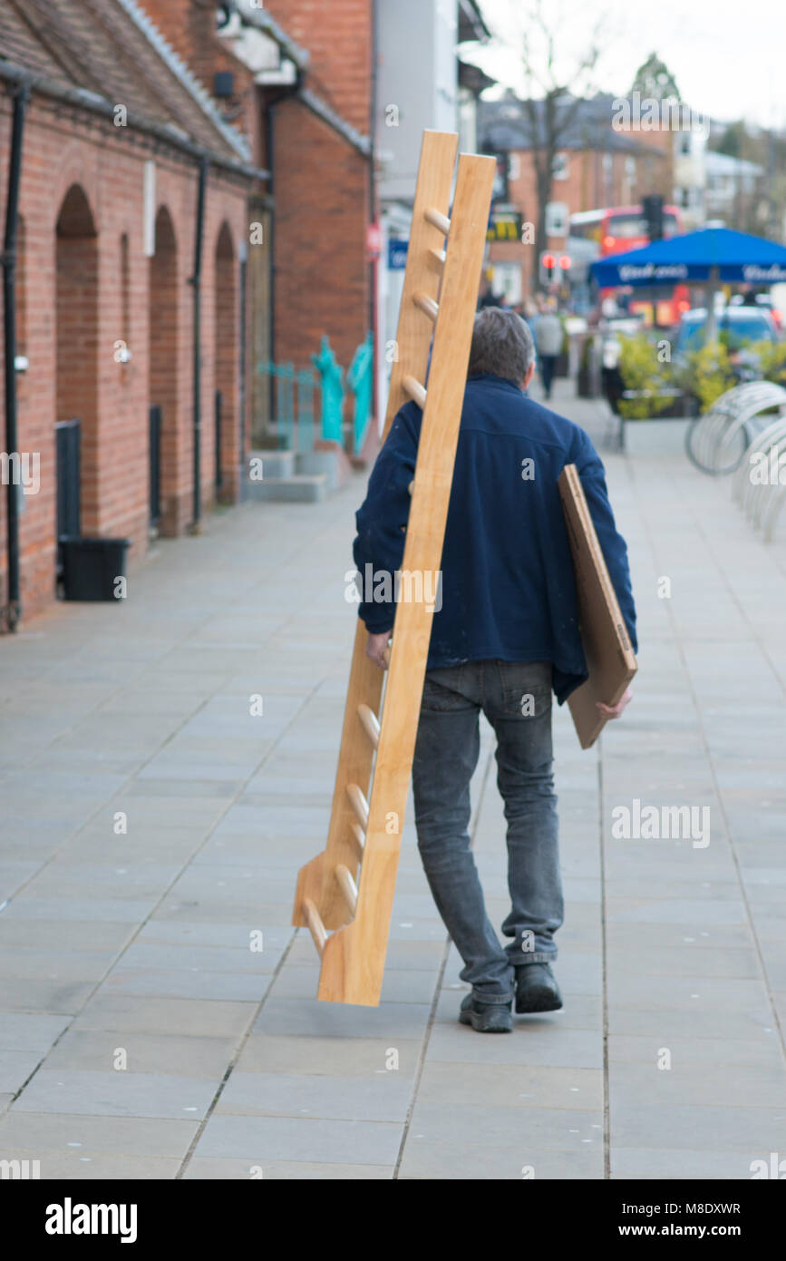 man carrying wooden ladders and flatpack along pavement sidewalk in ...