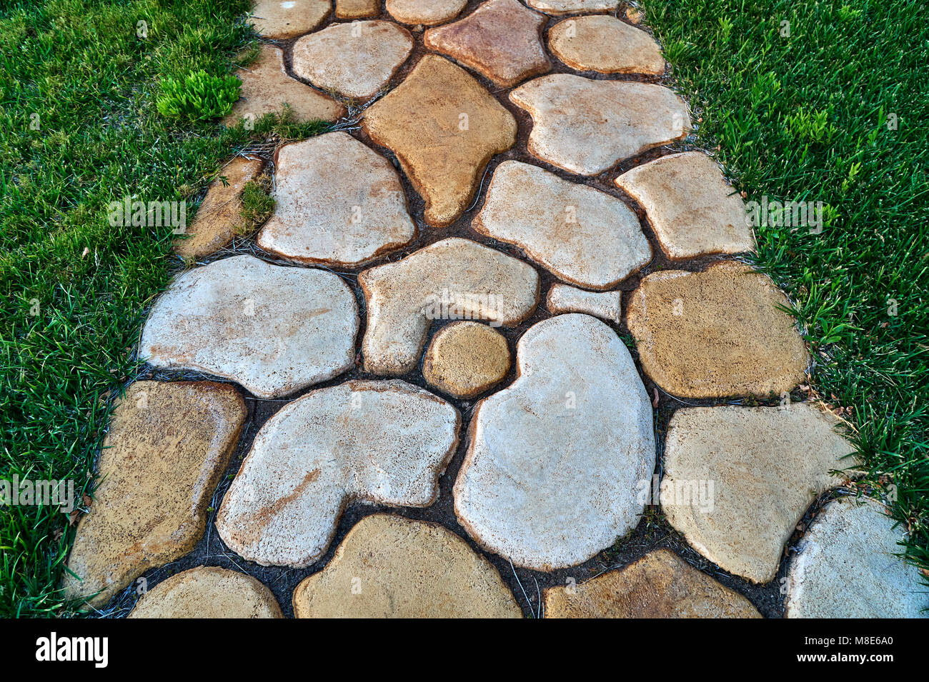 Elegant narrow road made with shaped colored rocks across lush green ...