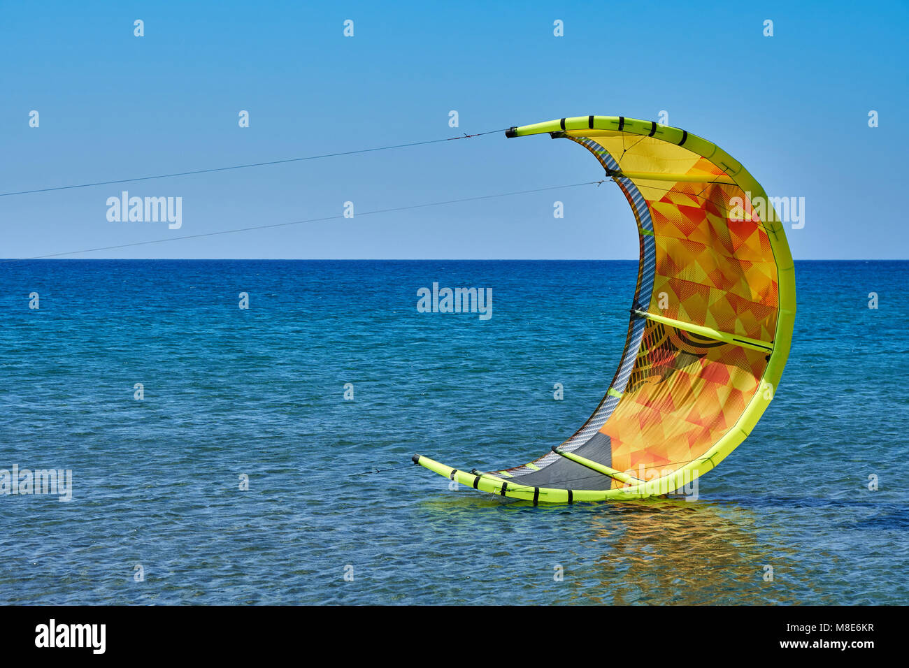 Bright yellow kite for surfing with ropes lies on tranquil ocean water ...