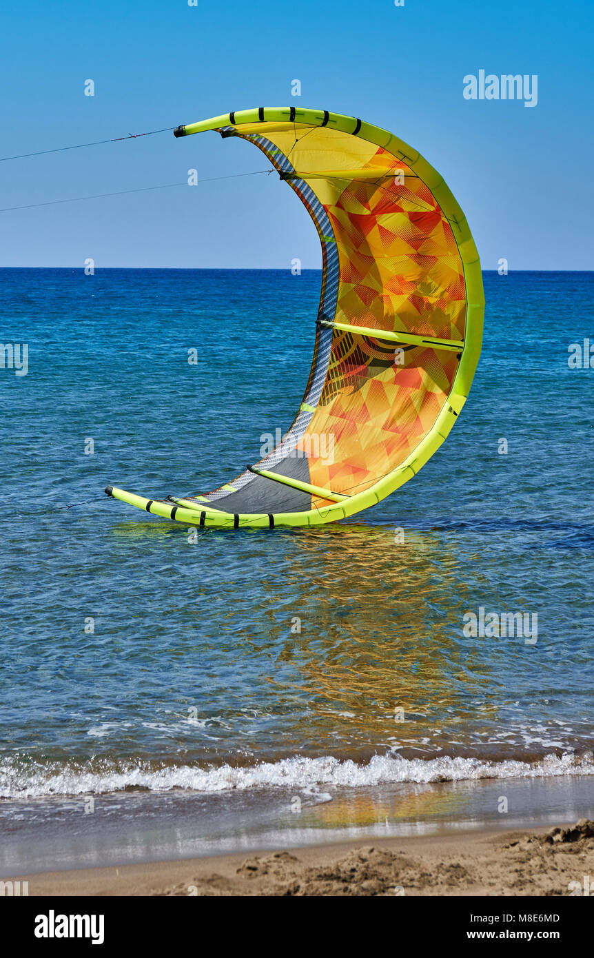 Bright yellow kite for surfing with ropes lies on tranquil ocean water ...