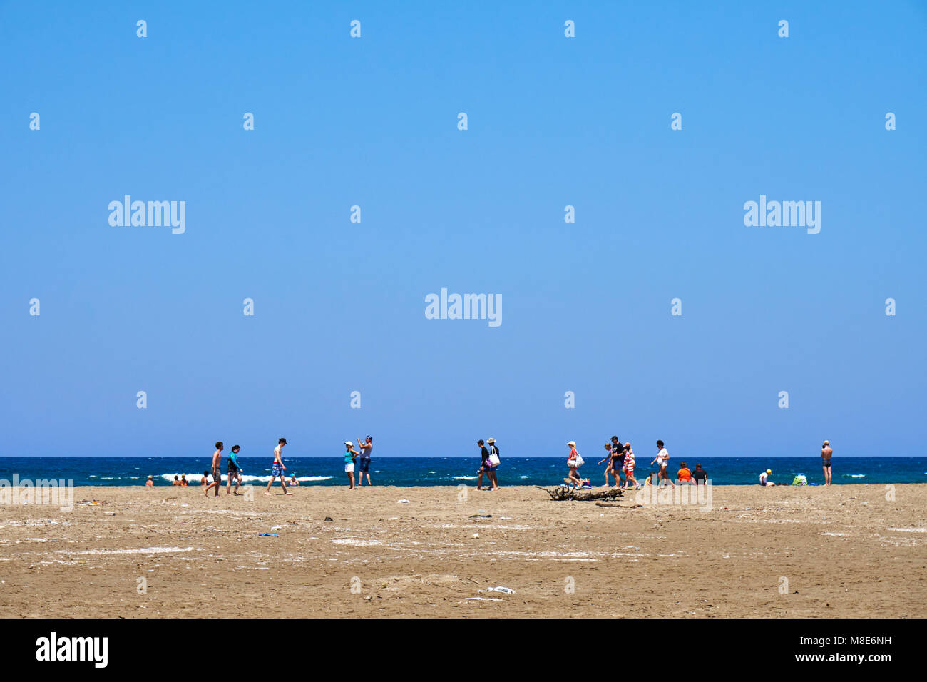 People in swimsuits and hats walk along the sandy beach against the ...