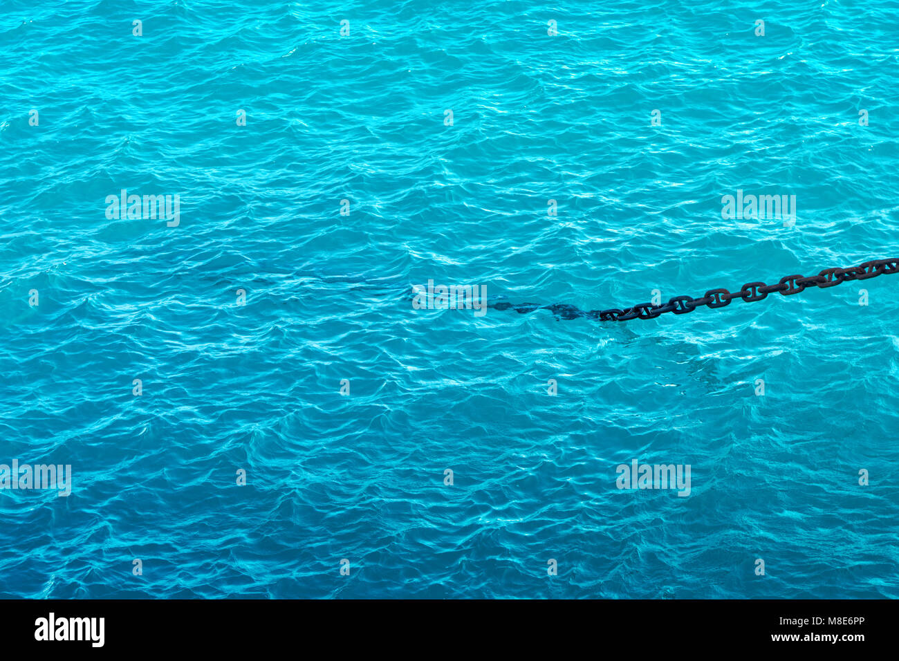 Anchor chain submerged on blue sea water with small waves under bright ...