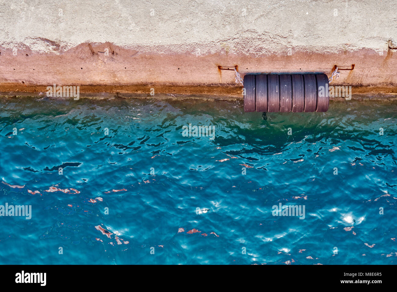 Large old tires of black colour hang on concrete pier edge to protect ...