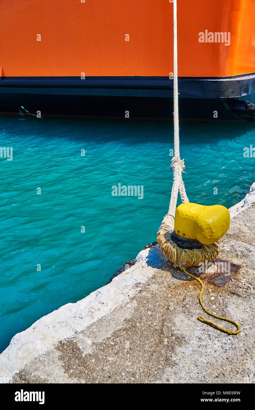 Yellow metal mooring bitt with large rope against orange vessel board ...