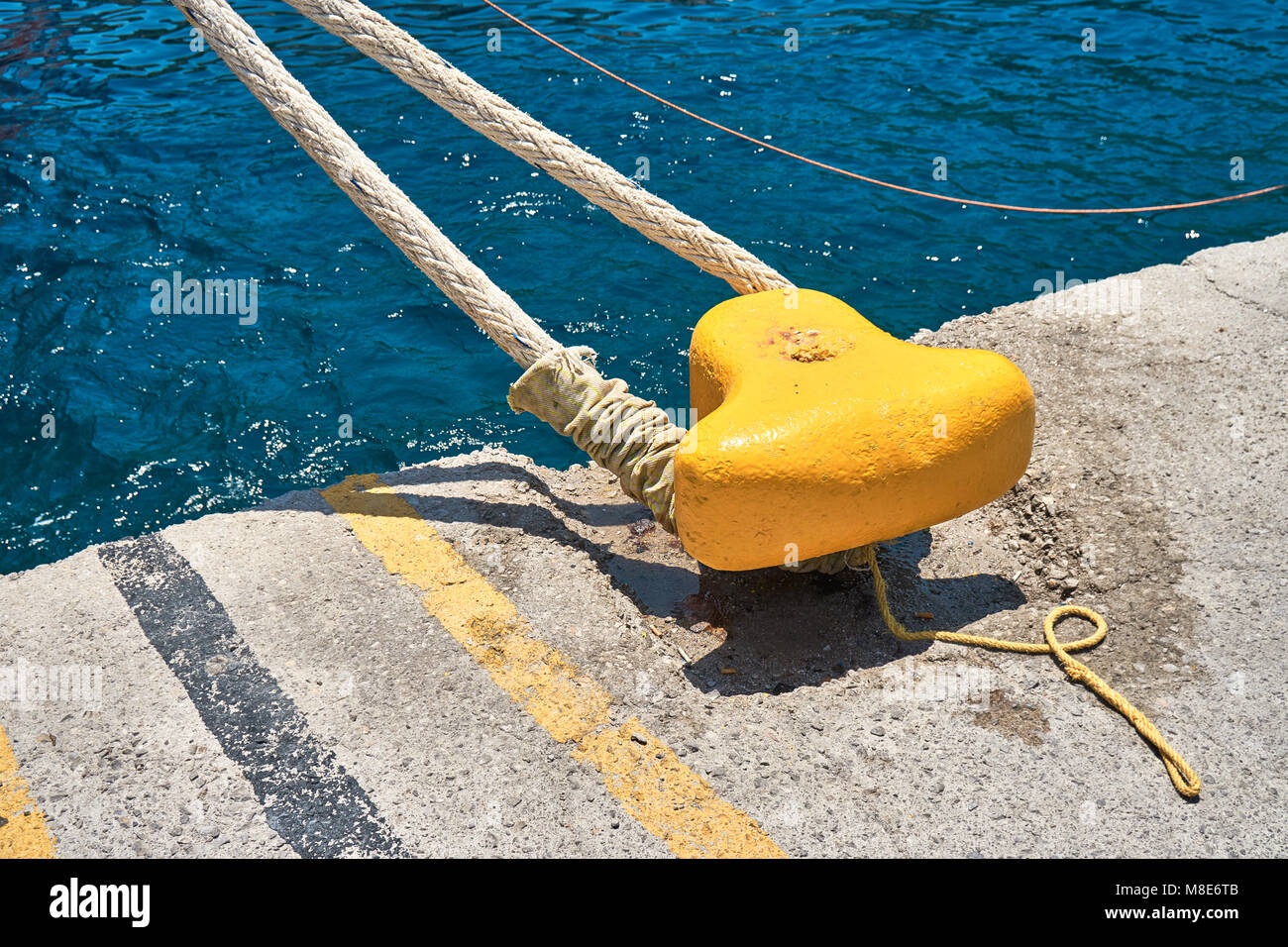 Yellow mooring bitt with rope on grey concrete pier at blue sea water ...
