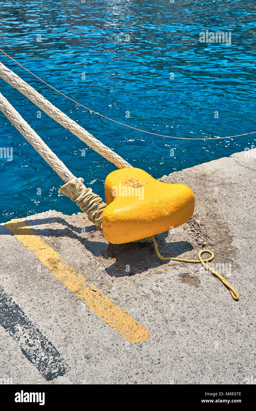 Yellow mooring bitt with rope on grey concrete pier at blue sea water ...