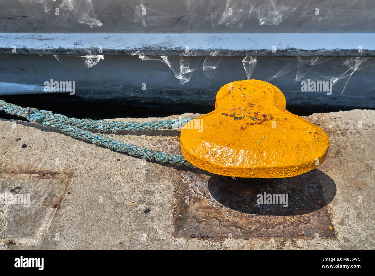 Yellow mooring bitt with rope on grey concrete pier at blue sea water ...