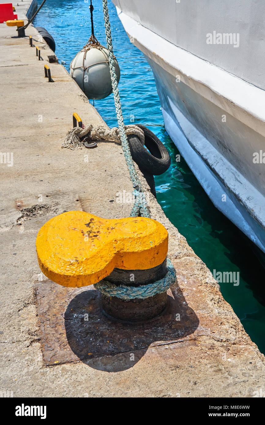 Yellow mooring bitt with rope on grey concrete pier at blue sea water ...
