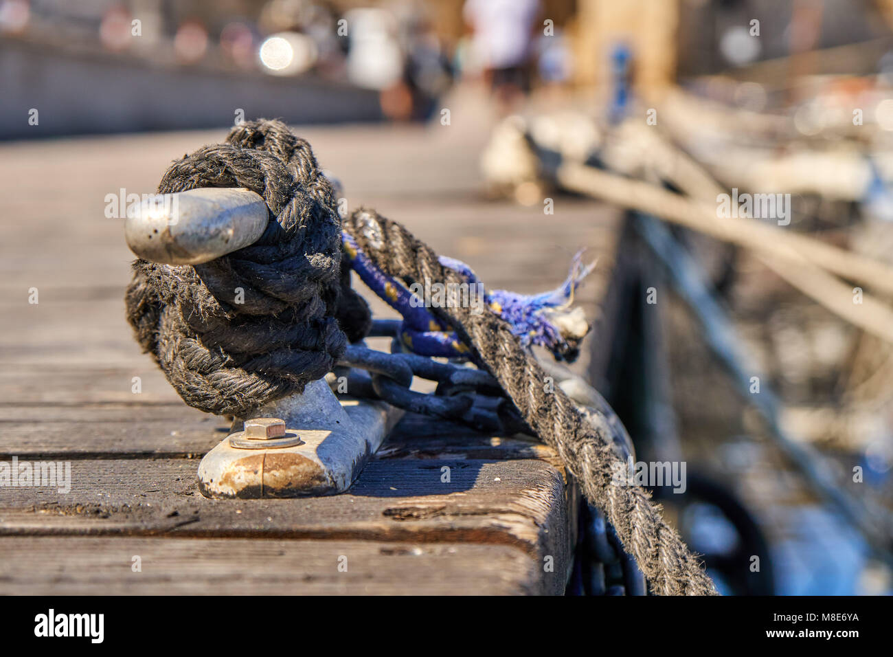 Metal mooring bitt with rope on wooden pier at blue sea water under ...