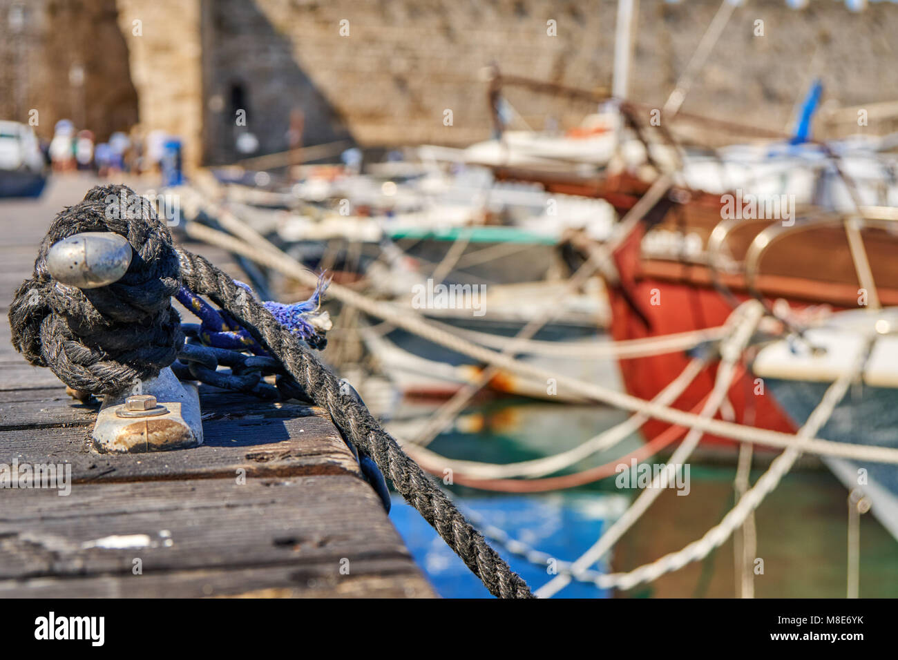Metal mooring bitt with rope on wooden pier at blue sea water under ...