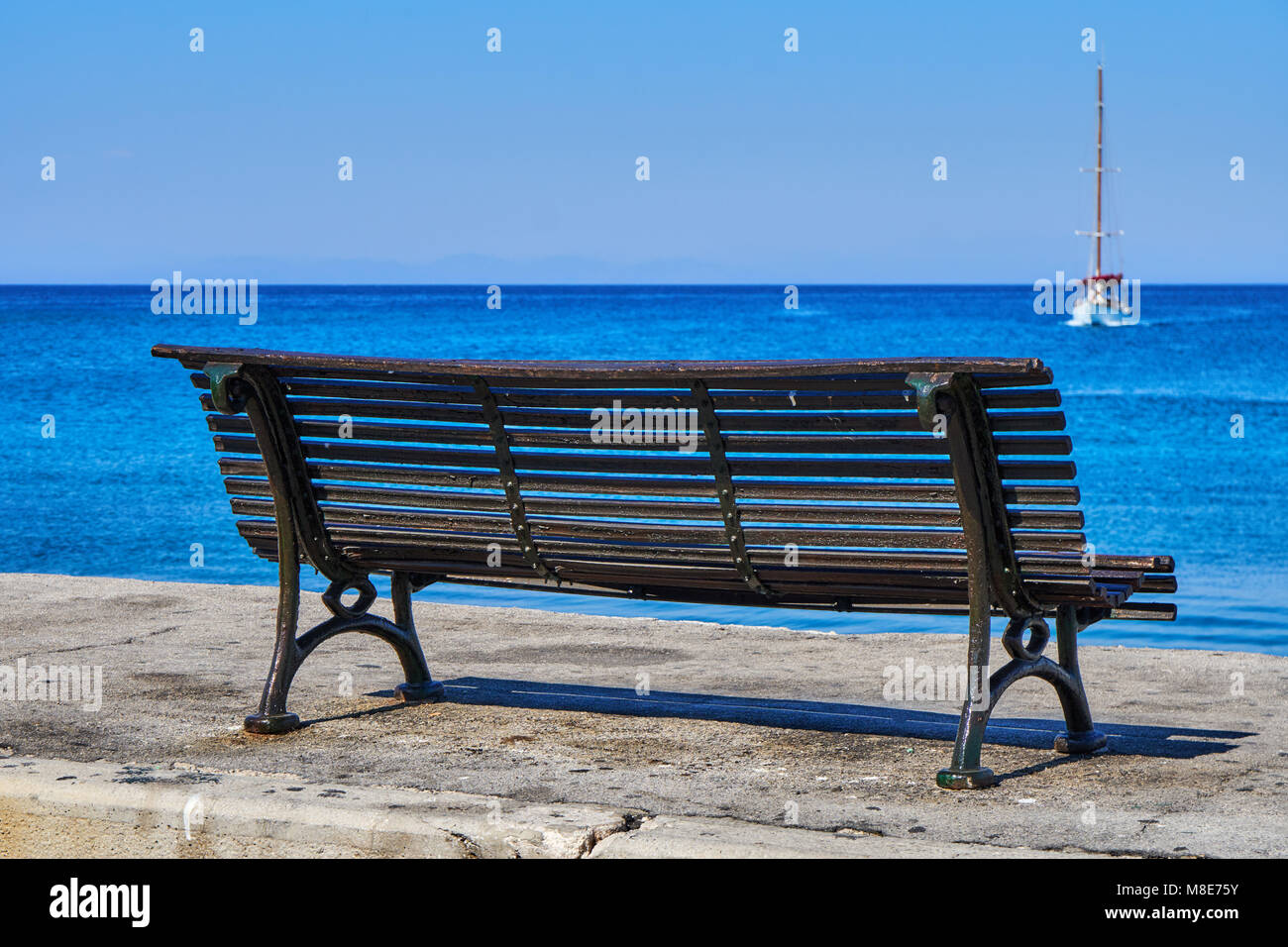 Bench standing on a promenade and a floating yacht Stock Photo - Alamy
