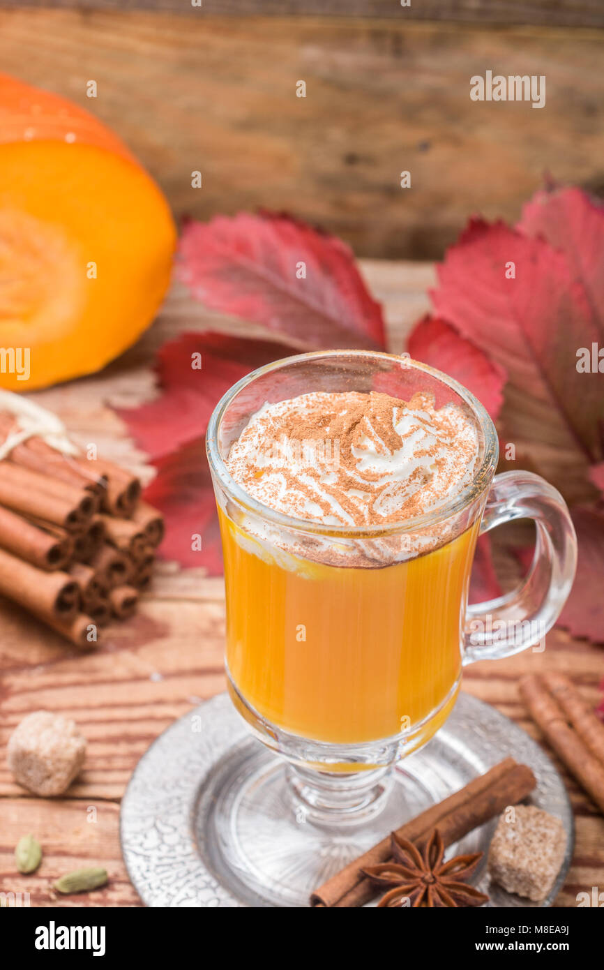Pumpkin spice latte smoothie with whipped cream and cinnamon in glass Cup on wooden background ...