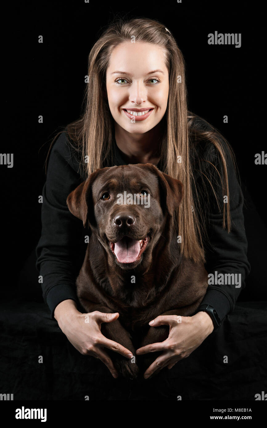 The young woman hugging black Labrador dog taken against black backdrop ...