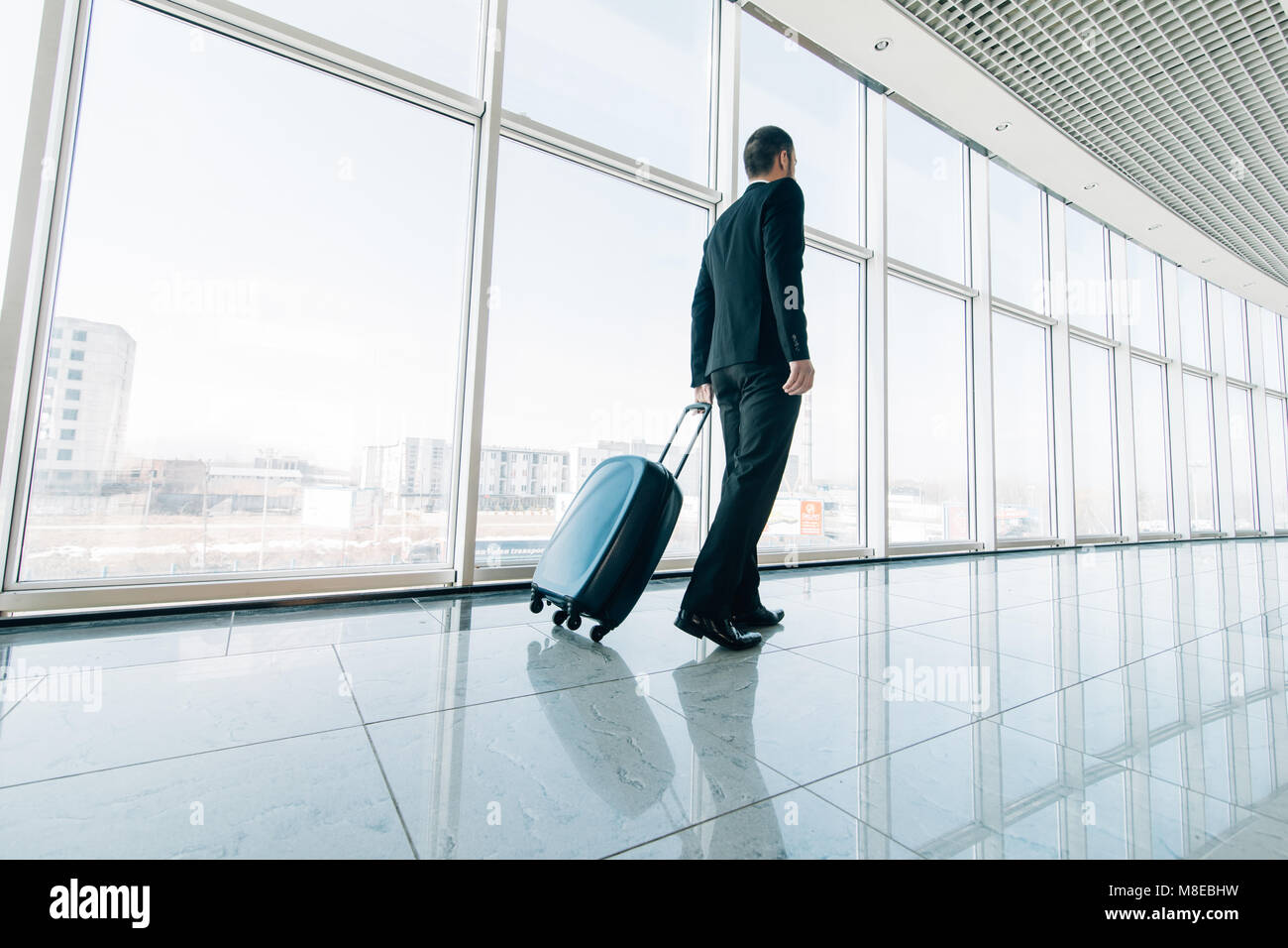 Young man pulling suitcase in modern airport terminal. Travelling guy ...