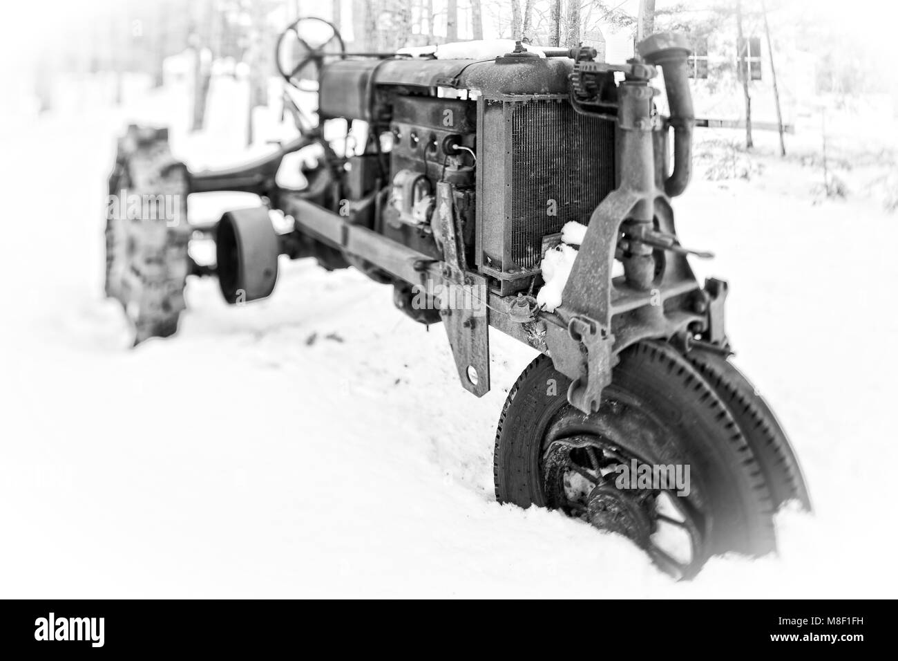 Tilt shift photograph of an old rusty steel wheel tractor in the snow ...