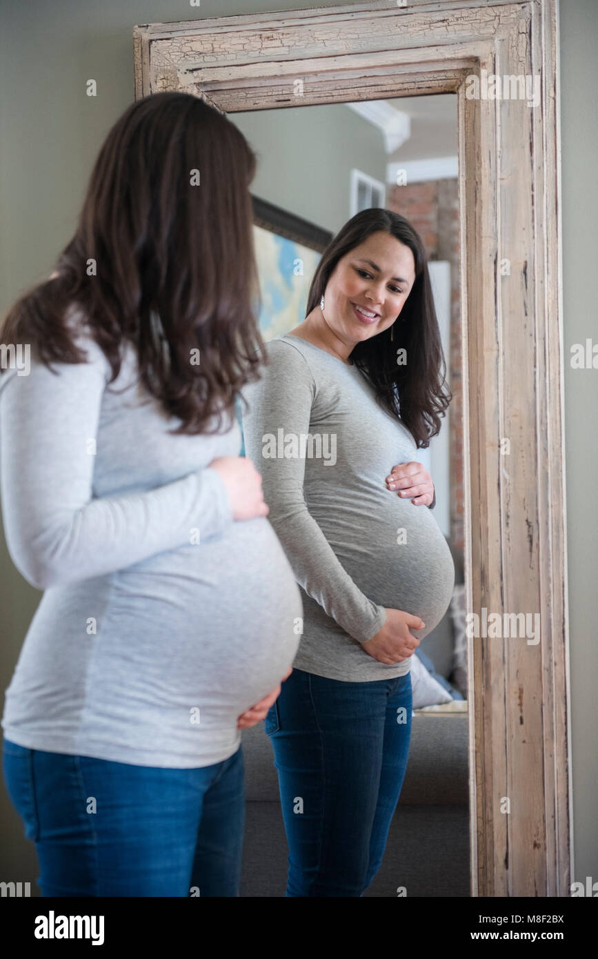 Pregnant woman looking in mirror, touching belly Stock Photo - Alamy
