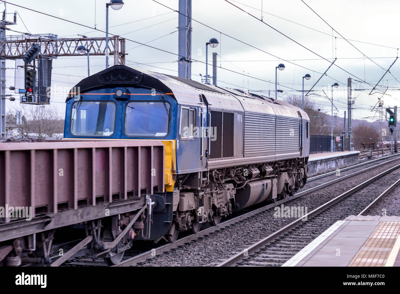 A freight diesel locomotive pulls a train of low sided metal bogies ...