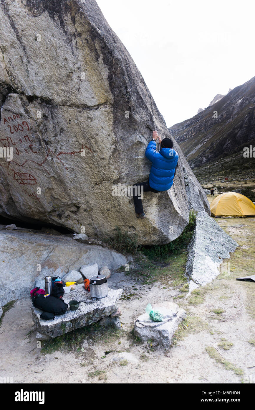 male mountain climber in a blue down jacket attempting a highball ...