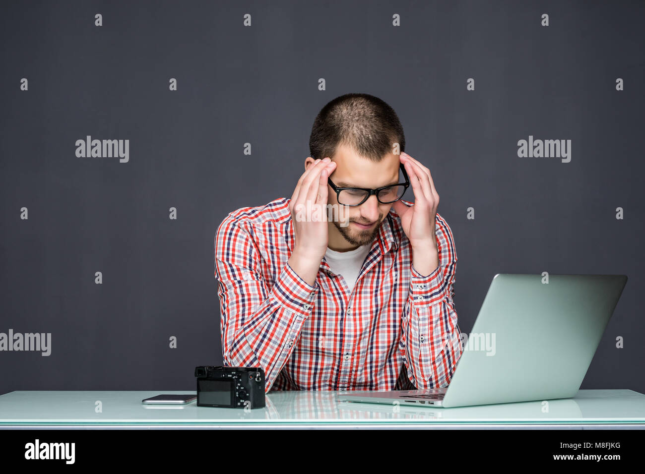 Pensive sad man sitting at the table with laptop over gray Stock Photo ...