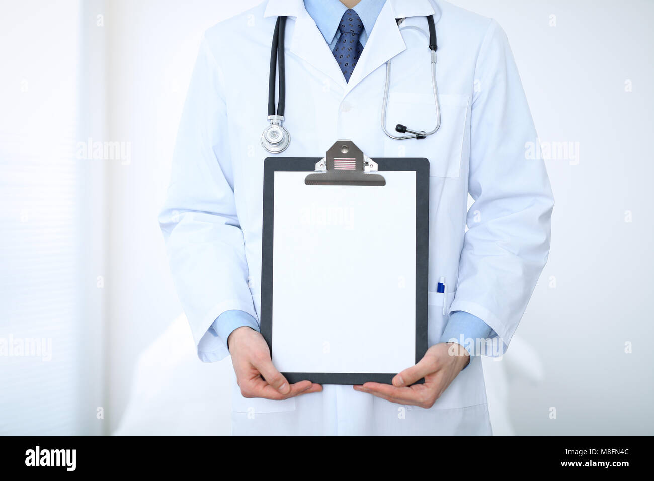 Unknown male doctor standing straight while holding medical clipboard ...