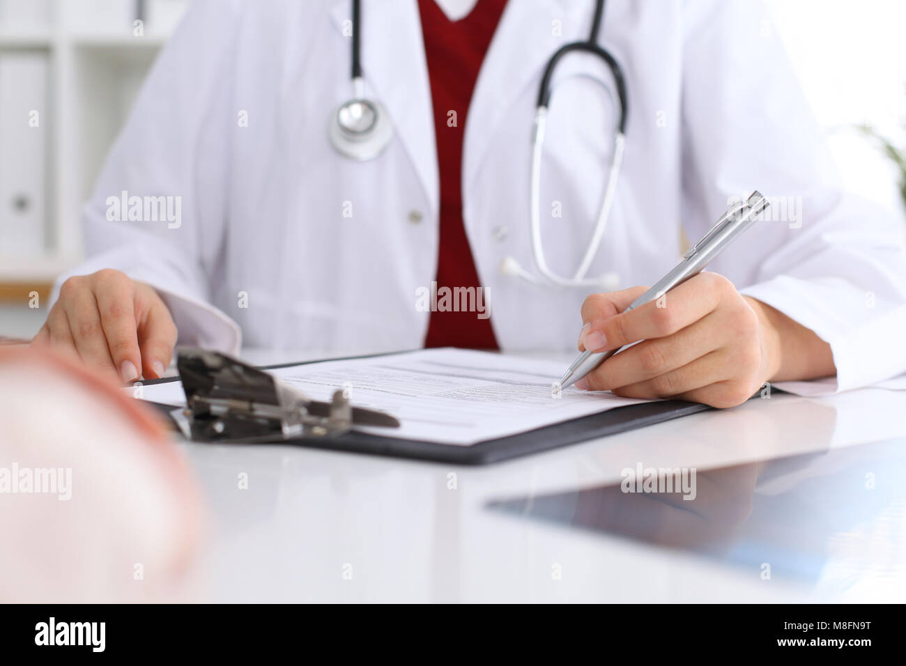 Close up of a female doctor filling up an application form while ...