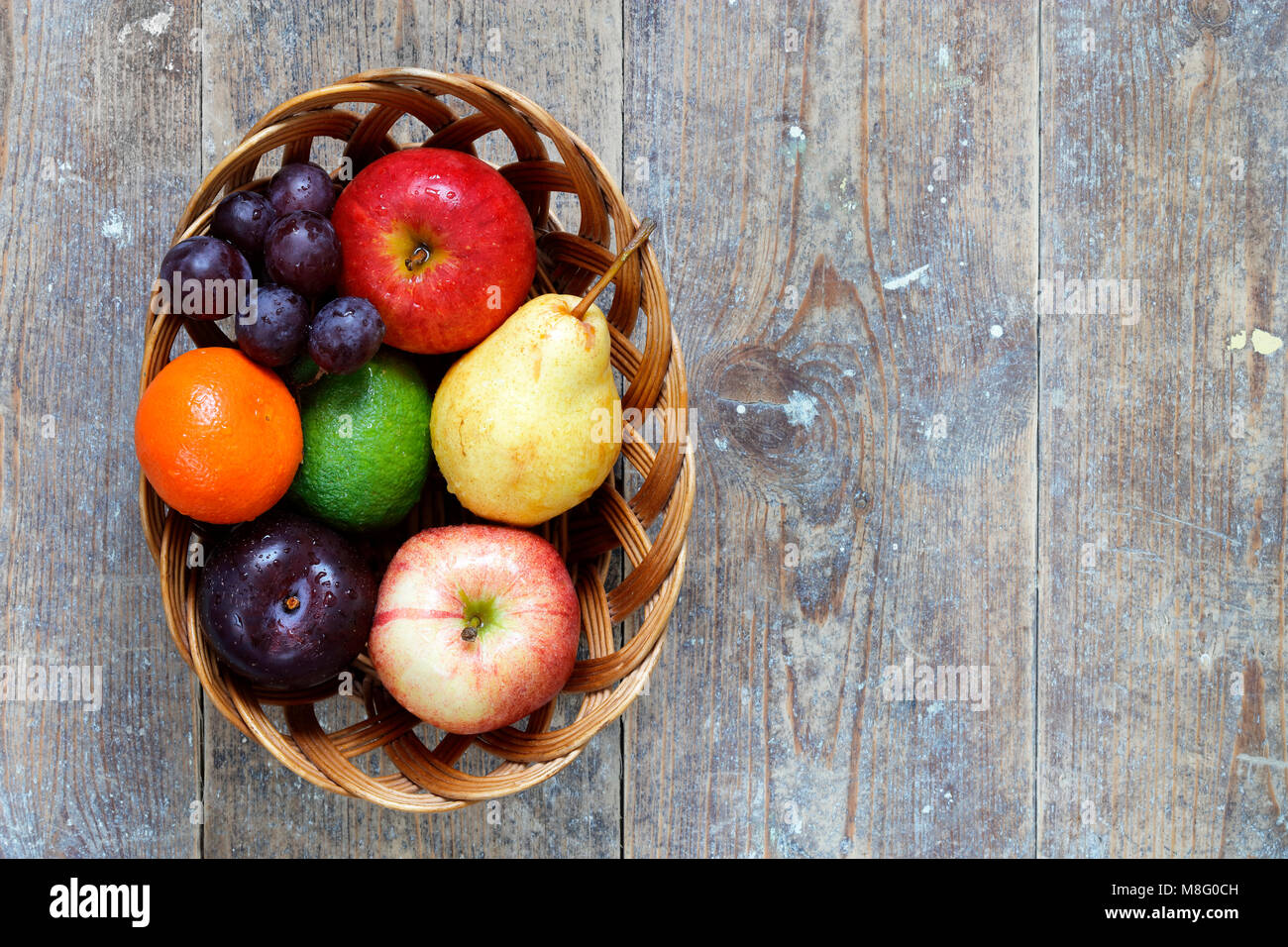Mixed fruits of apples, lime, lemon, pears and plums in wicker bowl on ...