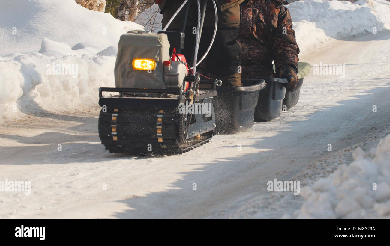 Man riding on crawler mini snowmobile with a trailer and a passenger on ...