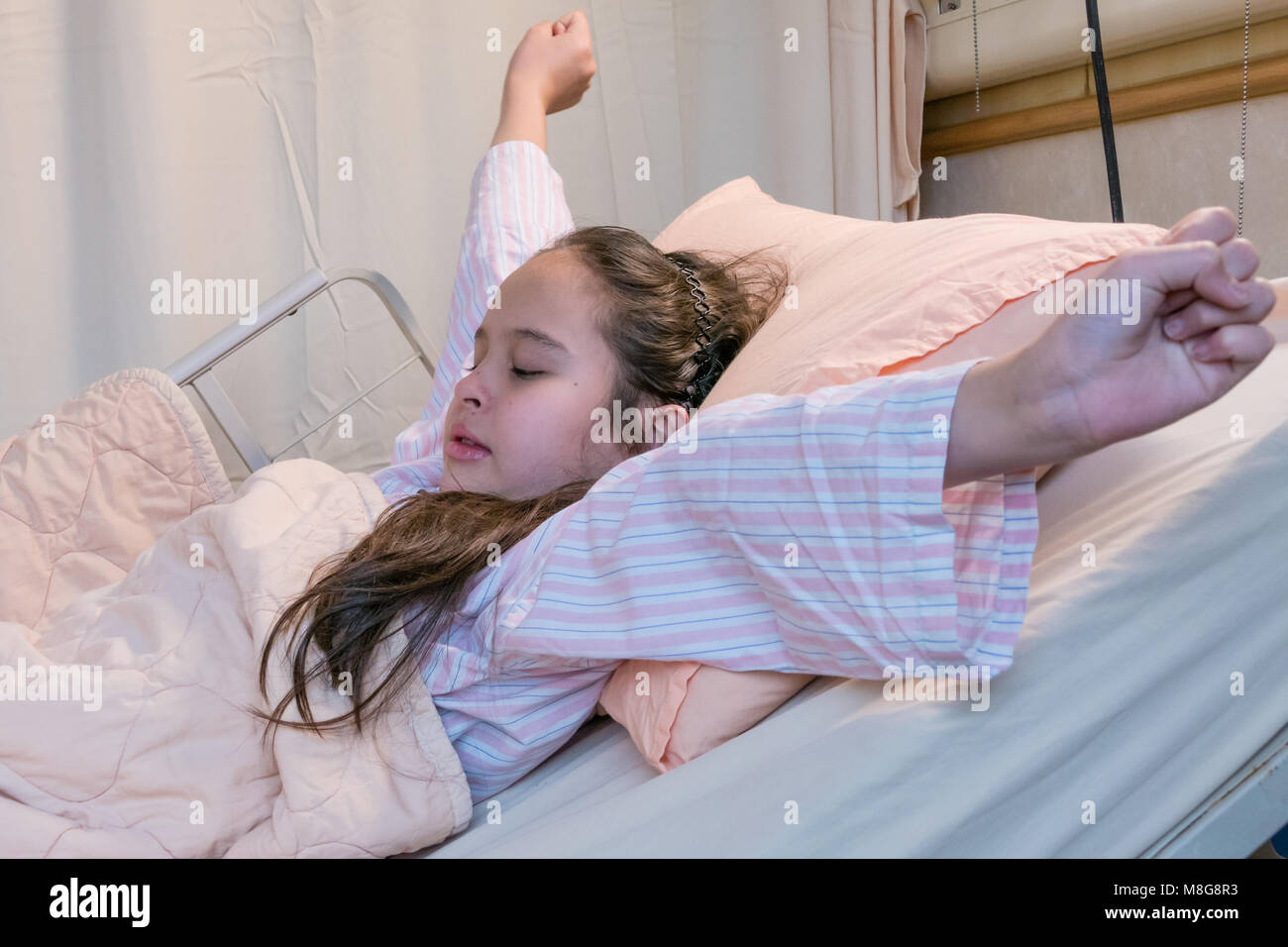 Mixed race Asian American tween girl stretching on hospital bed Stock ...