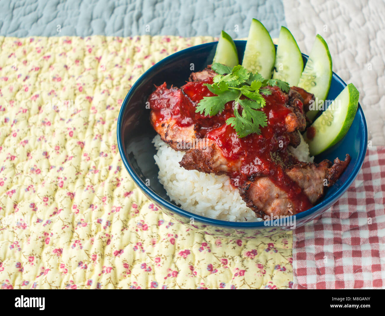 Fried pork on steam rice with sliced cucumber and parsley in blue bowl ...