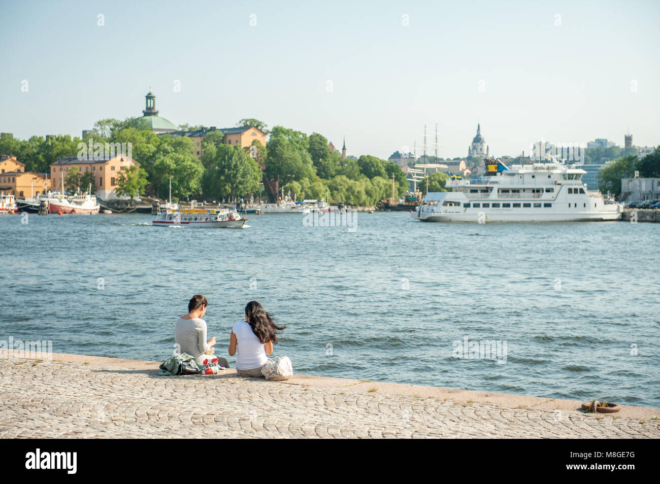 Tourists enjoy a picnic at Nybroviken waterfront in Stockholm. The city ...