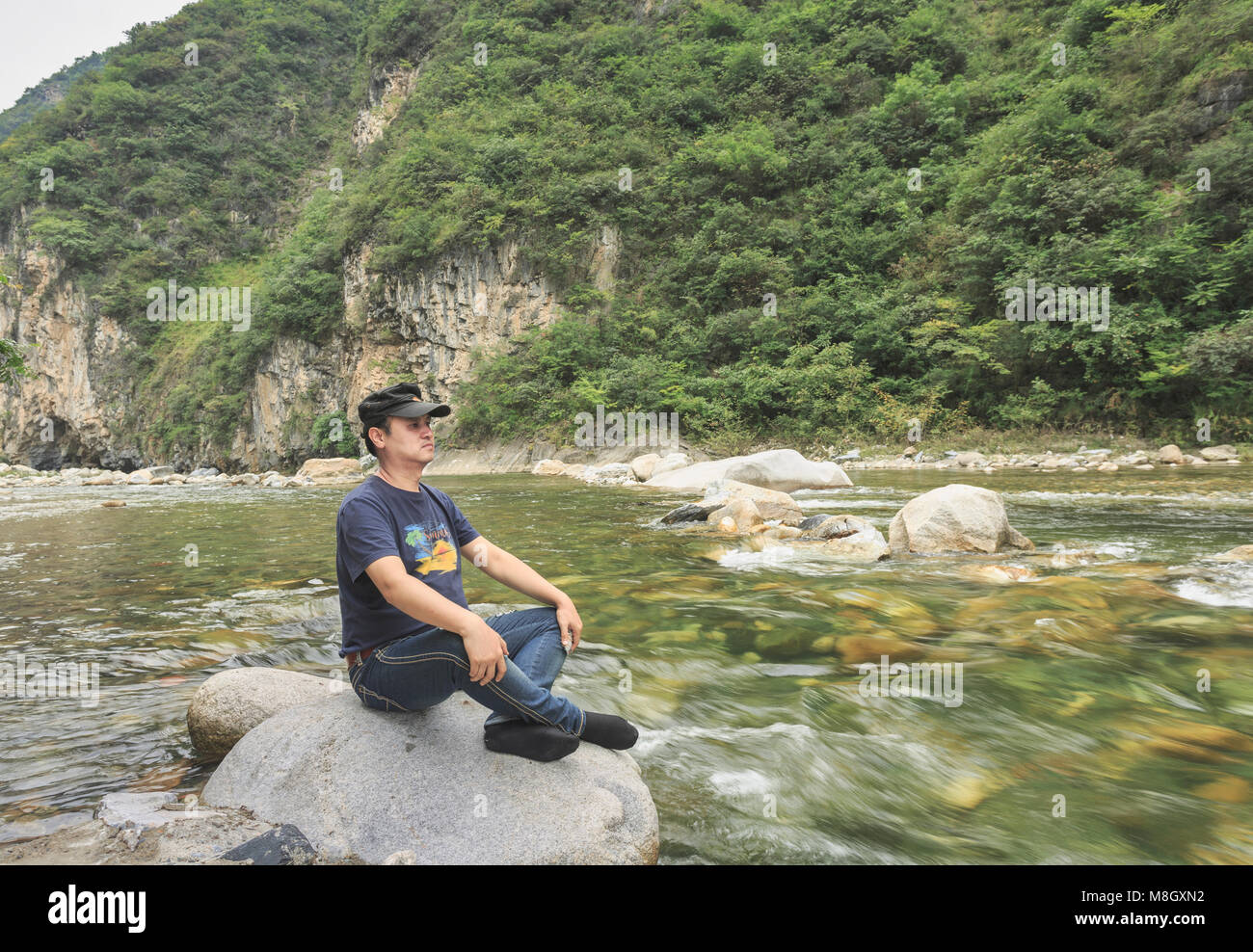 A Chinese man sitting on a big stone in the stream Stock Photo - Alamy