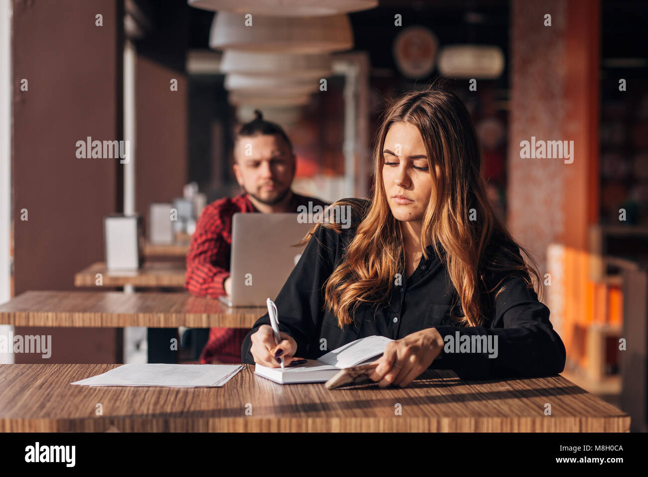 business young girl writing note in notebook in cafe, man with laptop ...