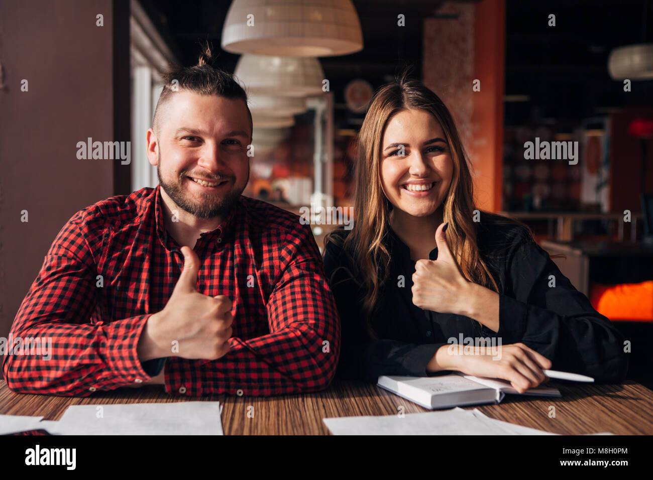two happy freelancers smile at the camera in cafe finger up, good job ...