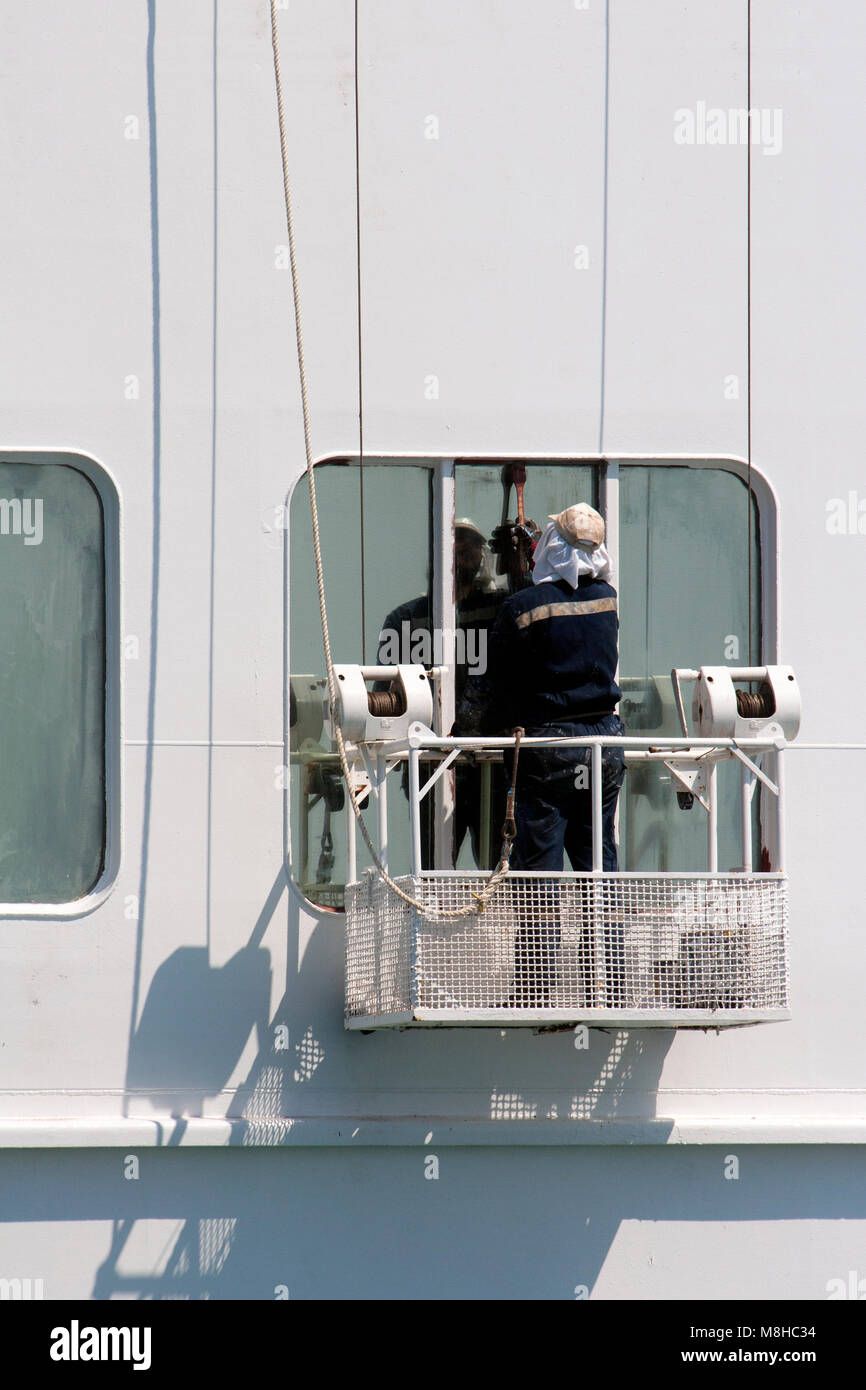 Man in the hanging platform cleaning windows of big passenger ship ...