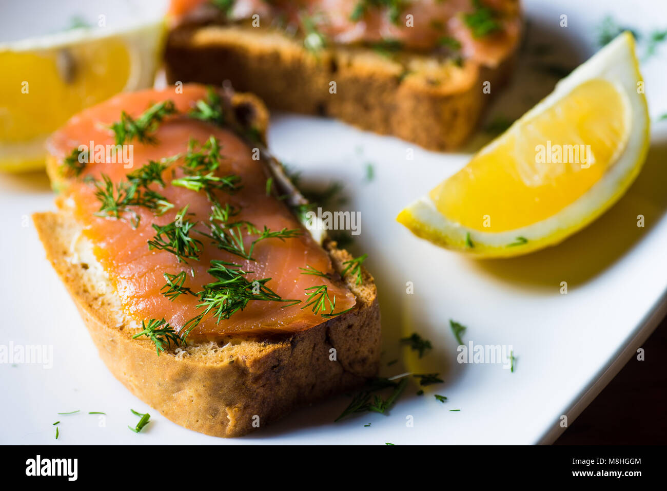 Toast with salmon, herbs and lemon on white plate Stock Photo - Alamy