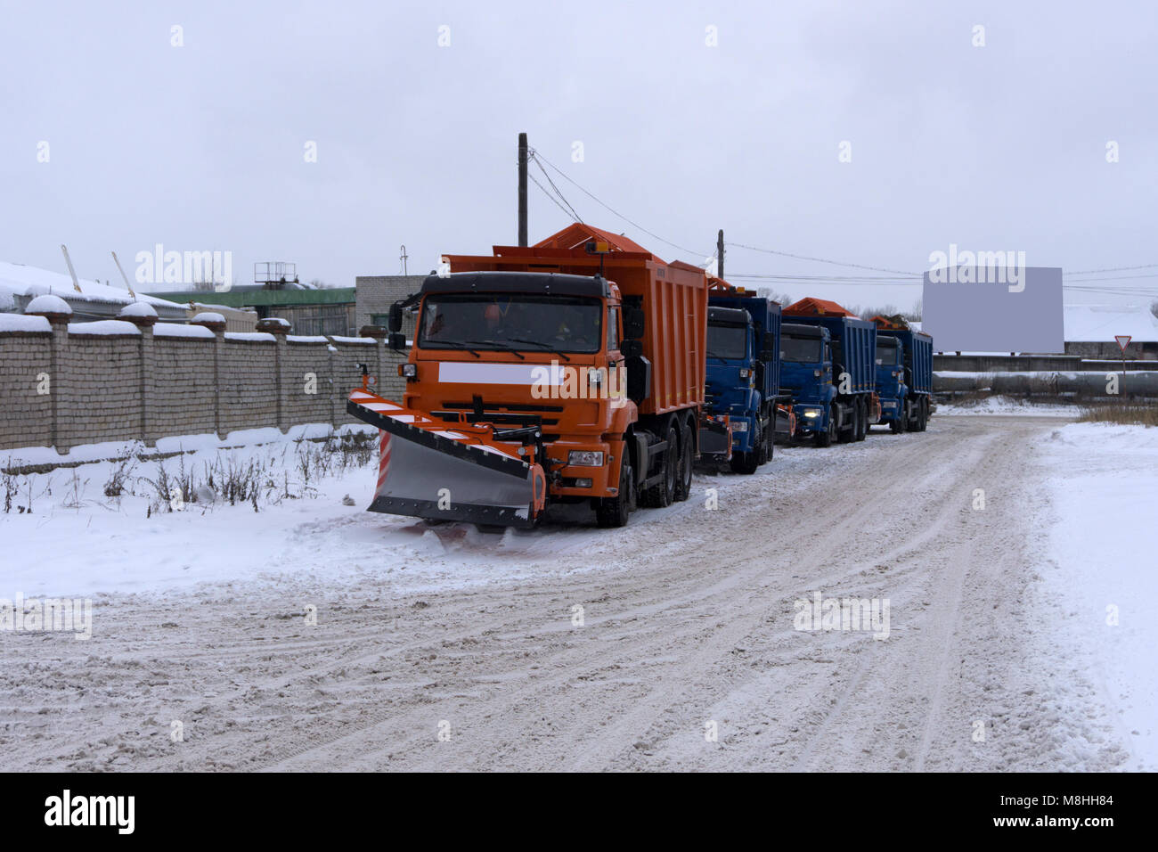 A column of five snow-remover trucks on the road in winter during a ...