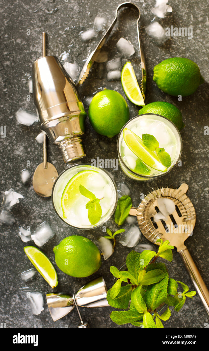Mojito cocktail with lime and mint in glass on a stone table. Bar tools ...