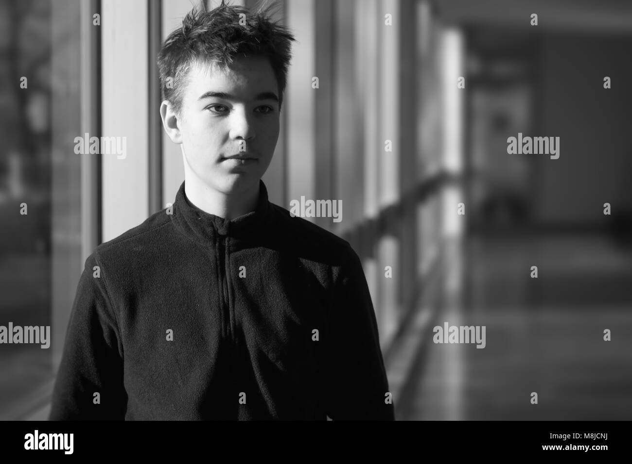 Boy portrait, dramatic shadow splits face of the teenager. Black and ...