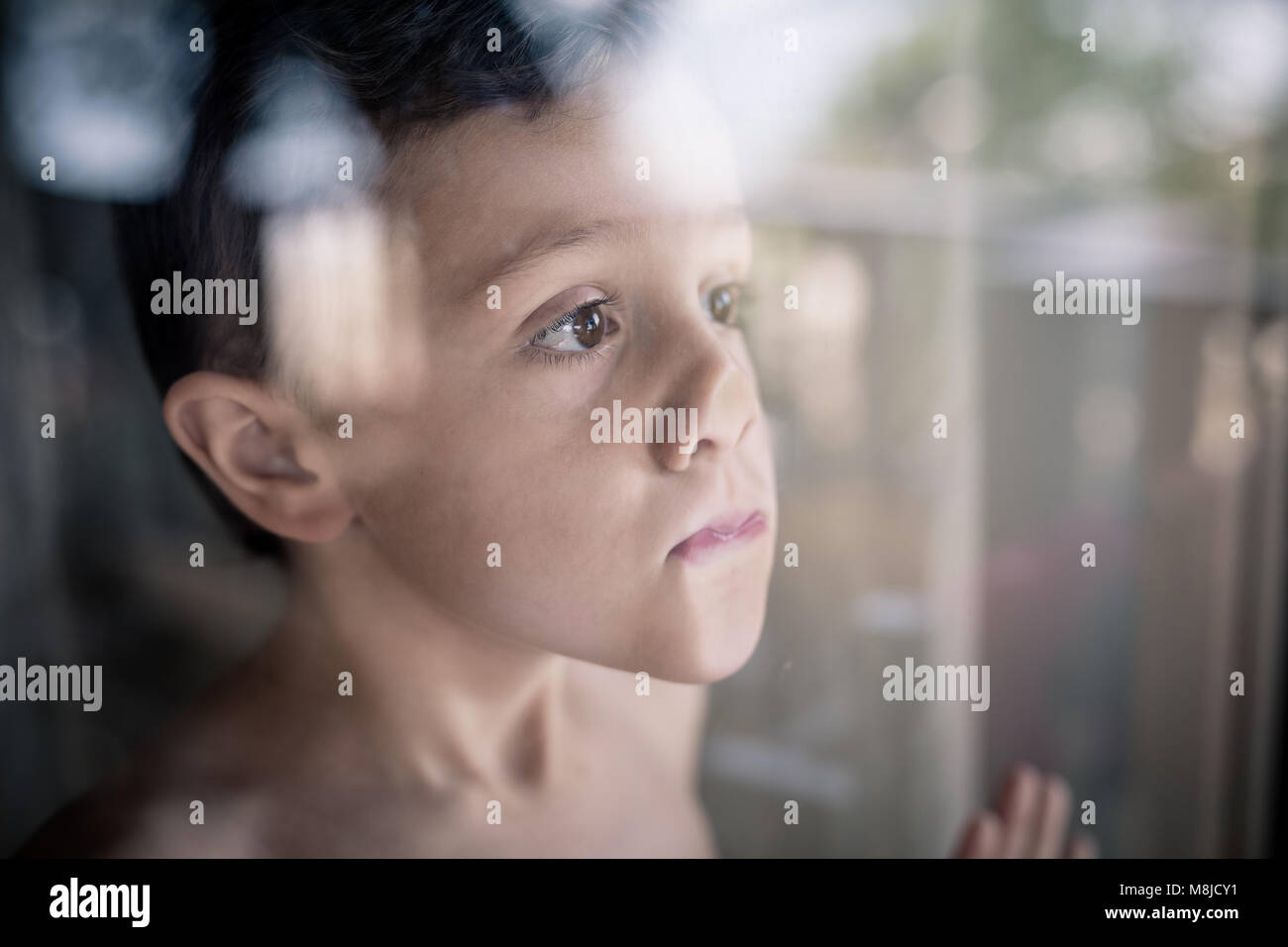 one sad little boy standing near the window at the day time. Concept of ...