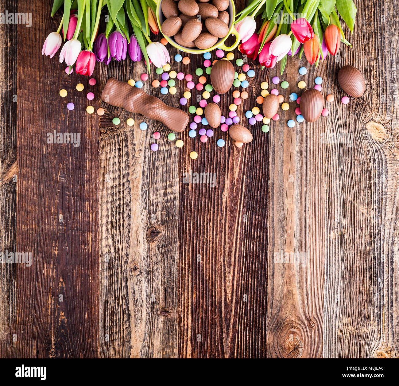 Easter wooden background with chocolate rabbit, easter eggs and tulips ...