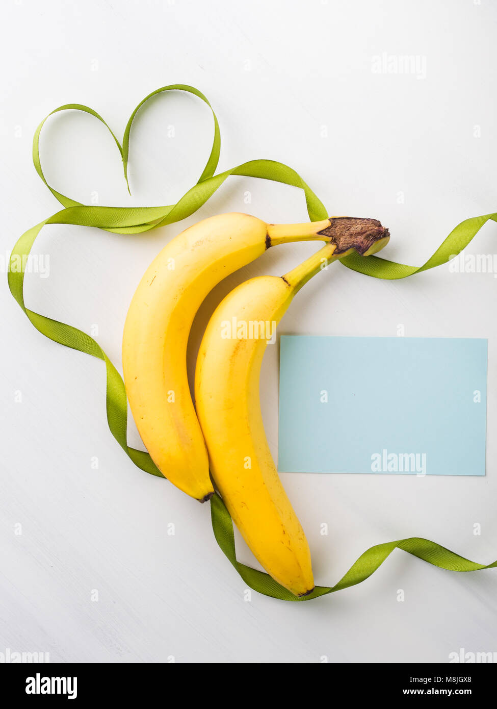 Two bananas with green ribbon frame and heart symbol on white ...
